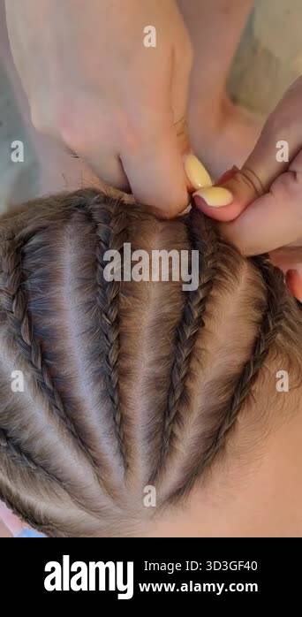 Vertical, Top-down close-up of professional hairstylists hands creating tight cornrow braids on ...