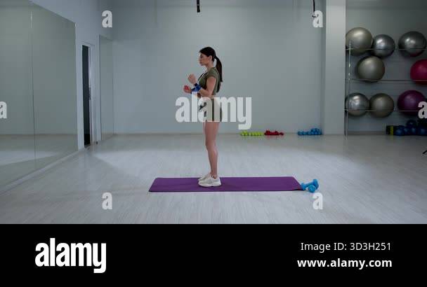 athletic woman stands on a purple exercise mat while doing band pull ...