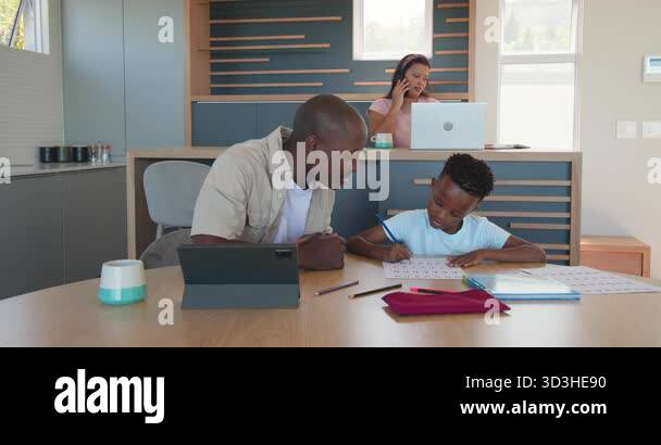 African american father and son doing homework at kitchen table, diverse mother with laptop, at ...