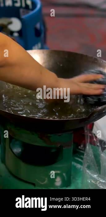 young woman in brown apron washes burnt frying pan with washcloth ...