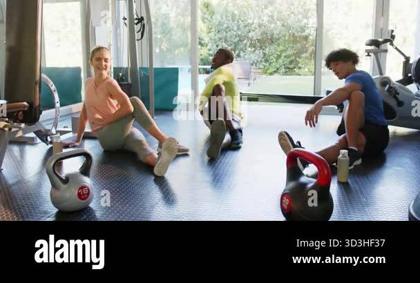 Young adults stretching on gym floor with kettlebell, focusing on ...