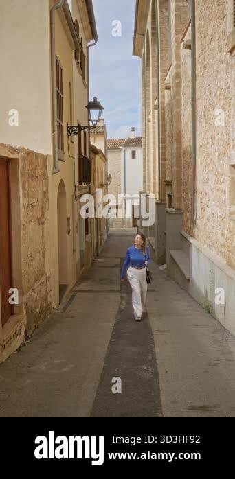 Woman walking through charming narrow street in mallorca's old town under clear skies, capturing ...