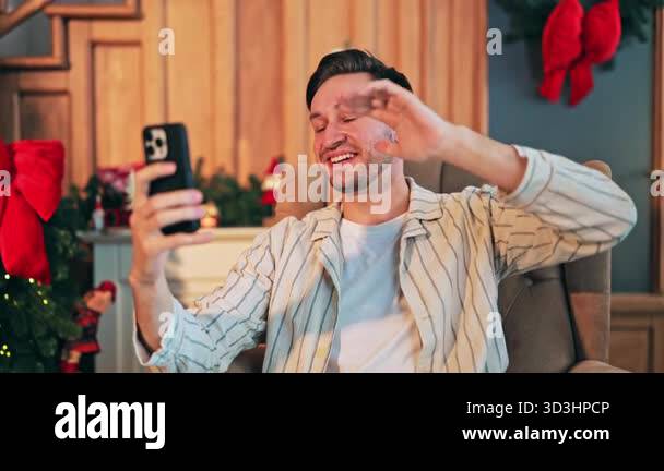 Happy individual enjoys Christmas video call on smartphone, sharing festive cheer. The man ...