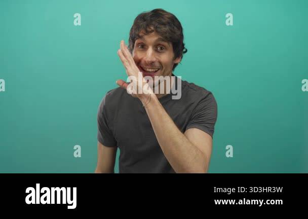 Young scruffy man cupping hand to mouth whispering in gray t shirt in ...