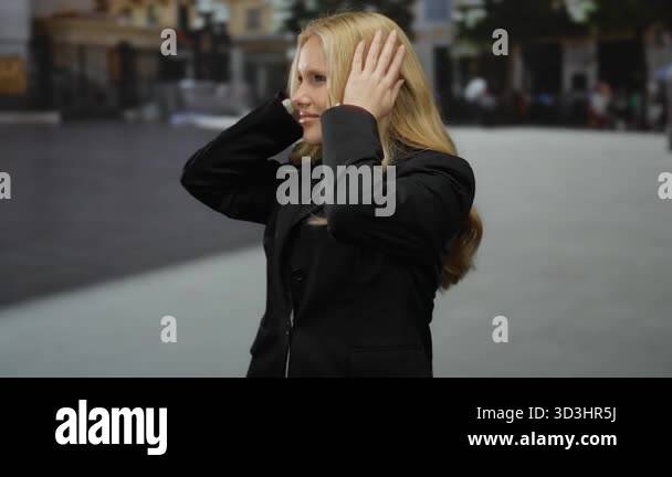 Blonde woman outdoors in city covering ears, expressing distress on ...
