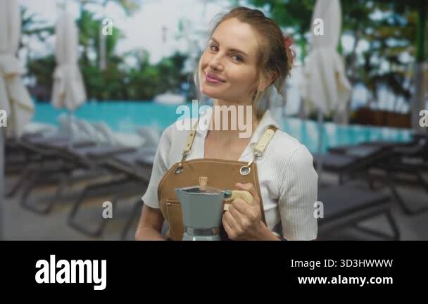 Woman in apron holding coffee maker by resort pool with palm trees and ...