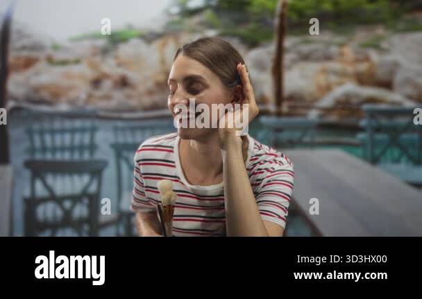 Woman holding paintbrushes cups ear with hand while smiling at a ...