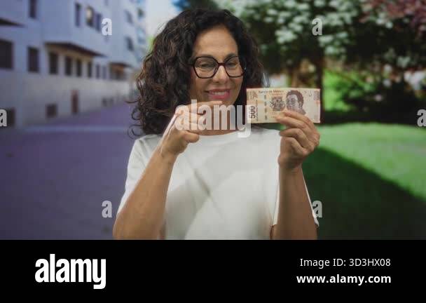 Woman smiling while holding mexican pesos in an urban outdoor setting ...