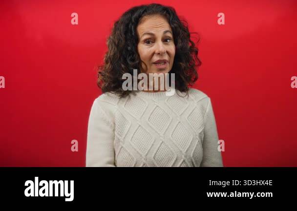 Mature hispanic woman with curly hair gestures on a vibrant red ...