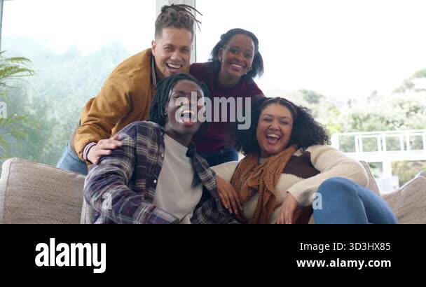 Diverse friends walking into living room, sitting on light-colored sofa ...
