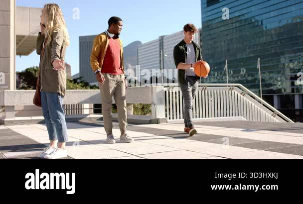 Diverse male friends dribbling basketball while walking past calling ...