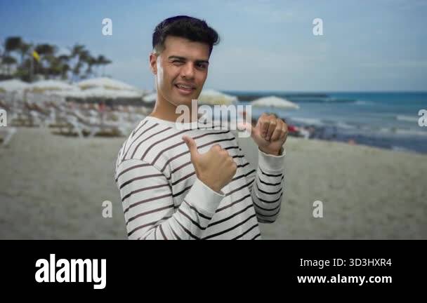 Young man smiles at beach, wearing striped shirt, with sea and ...