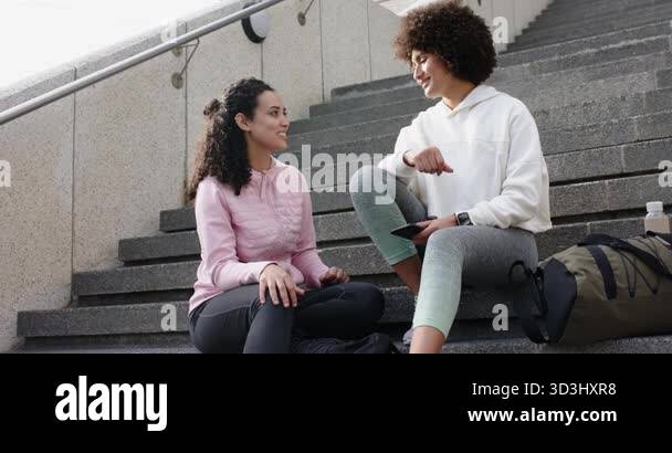 Diverse female friends tapping and swiping tablet at stone steps ...