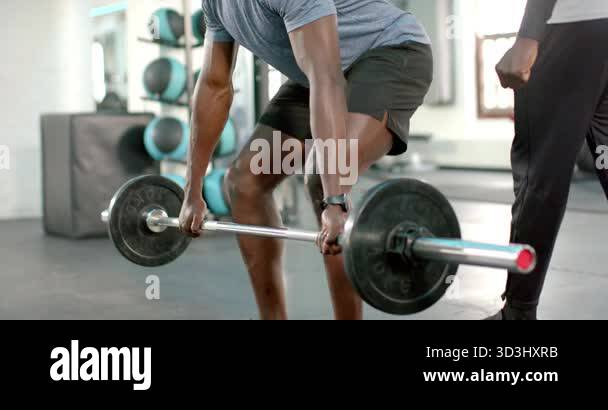 With trainer guiding, African American client deadlifting barbell for ...