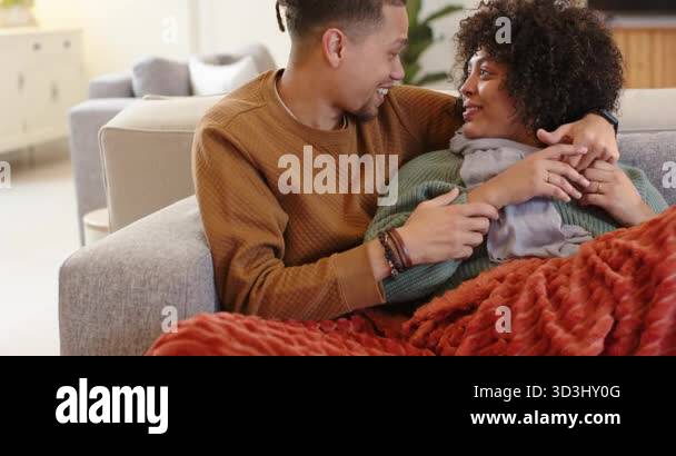 Couple leaning into embrace on sofa under red throw, man wrapping arm ...