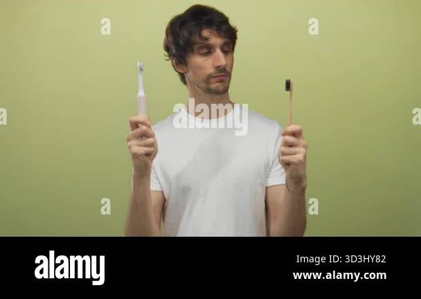 Young man holds electric toothbrush and bamboo toothbrush while ...