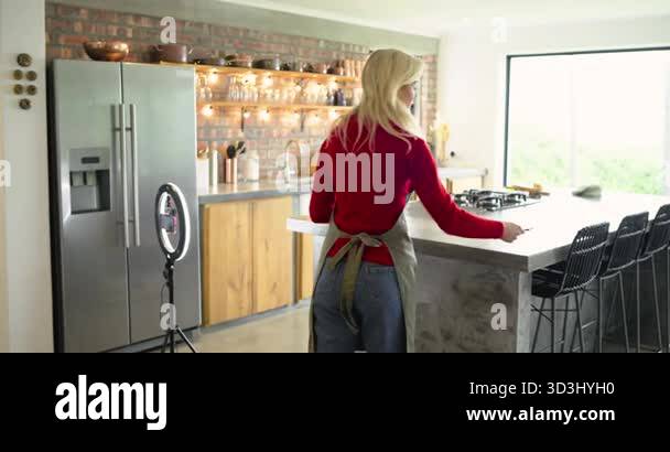 Woman entering kitchen, placing phone and adjusting ring light, showing ...