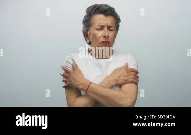 Senior woman with grey hair shivers in cold wearing a white shirt ...