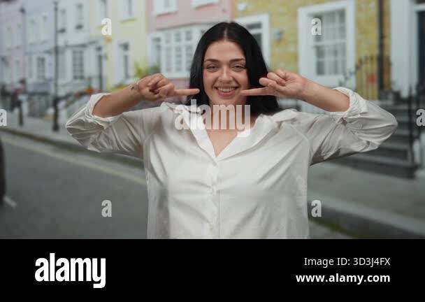 Young plus size woman smiles and points at her smile with fingers while ...