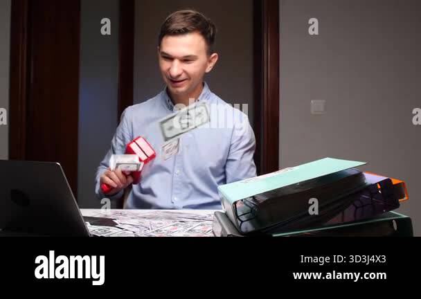 Happy man sitting at a desk shooting a money gun, celebrating wealth ...