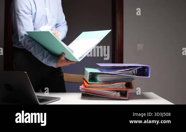 Man standing at a desk, checking and filing documents into an open ring ...