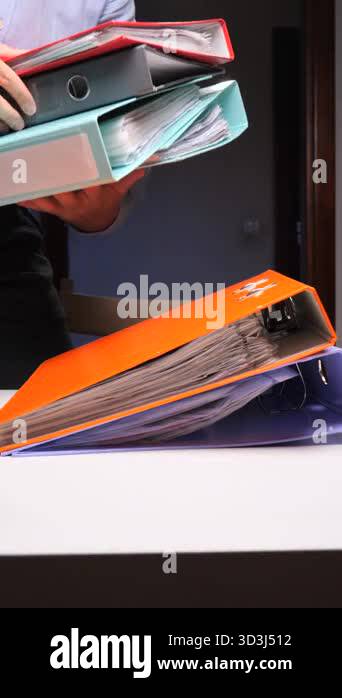 vertical video Person handles a towering stack of colorful ring binders overflowing with various ...