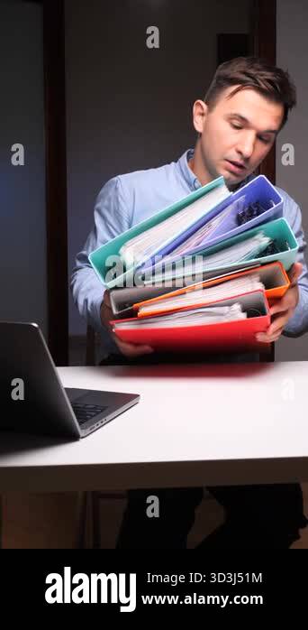 vertical video Stressed man looking down at a stack of colorful binders ...