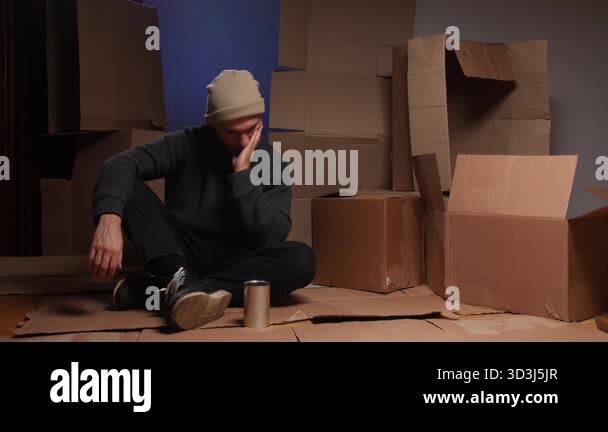 Homeless man sitting on cardboard boxes in improvised street shelter ...