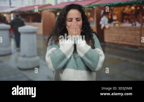 Woman sneezing in outdoor street market with wooden stalls, capturing a ...