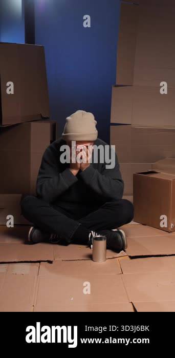 vertical video Homeless man sitting on cardboard boxes, covering his ...