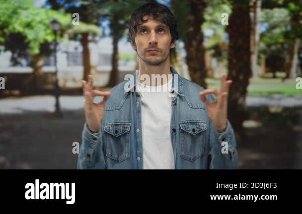 Man in blue denim jacket with hands pressed together in prayer pose ...