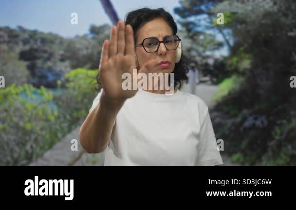 Middle age hispanic woman raises hand palm facing forward in a green ...