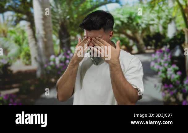 Young man with headphones covers his face playfully while standing in a ...