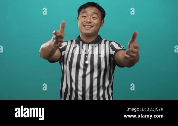 Man in striped referee shirt extends arms holding whistle in teal ...