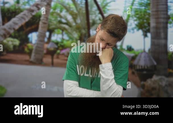 Man with beard wearing green volunteer t-shirt rests hand on cheek ...