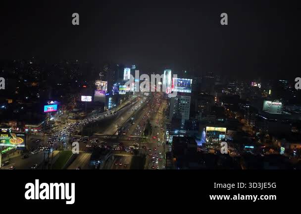 Aerial perspective of bustling highway in Lima, Peru, illuminated by vibrant billboards and city ...