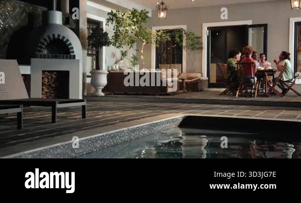 Tracking shot past swimming pool to happy diverse friends talking on ...
