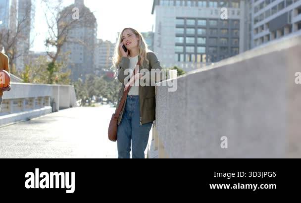 Woman walking onto walkway leaning on barrier calling smartphone ...