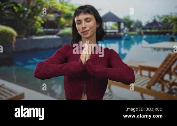 Young hispanic woman by a blue pool makes prayer gesture with pressed ...