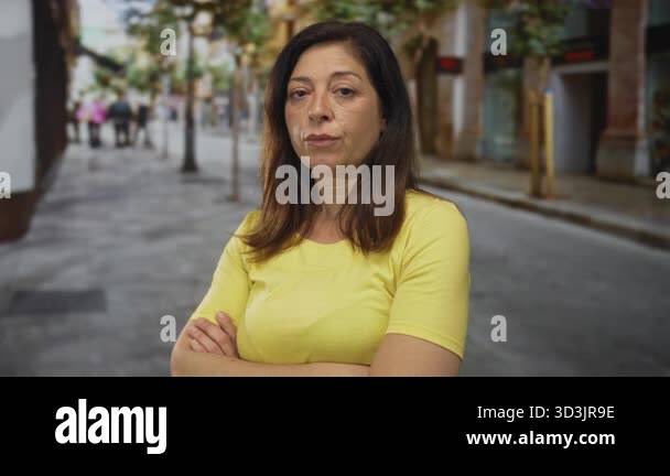 Woman with arms crossed and a steady gaze on a city street lined with ...