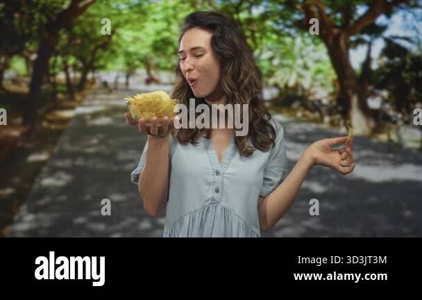 Woman eating a crispy potato chip from a glass bowl while holding it in ...