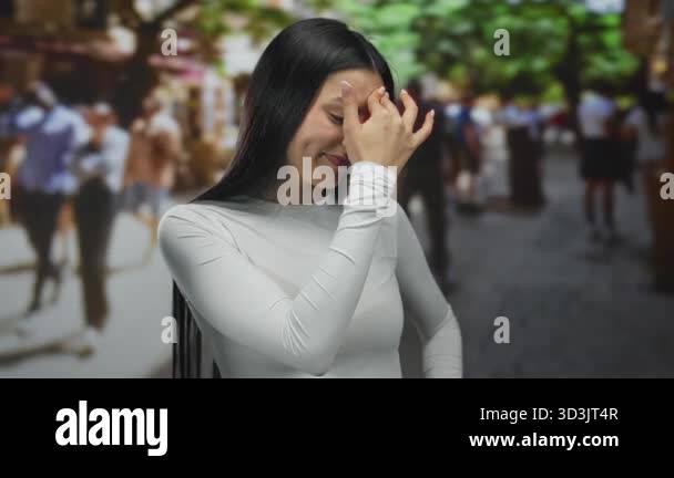Woman expressing concern on a bustling city street with blurred pedestrians around, showcasing ...