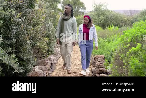 Pointing at shrubs, diverse couple walking wood-chip path and examining ...