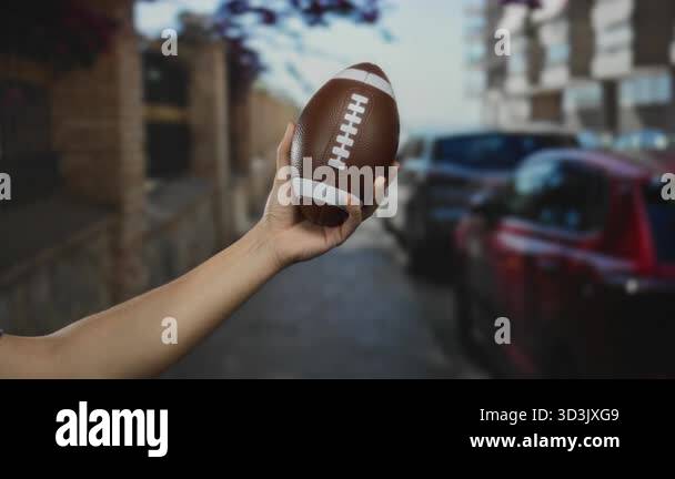 Man holding football on city street with cars and buildings in the ...