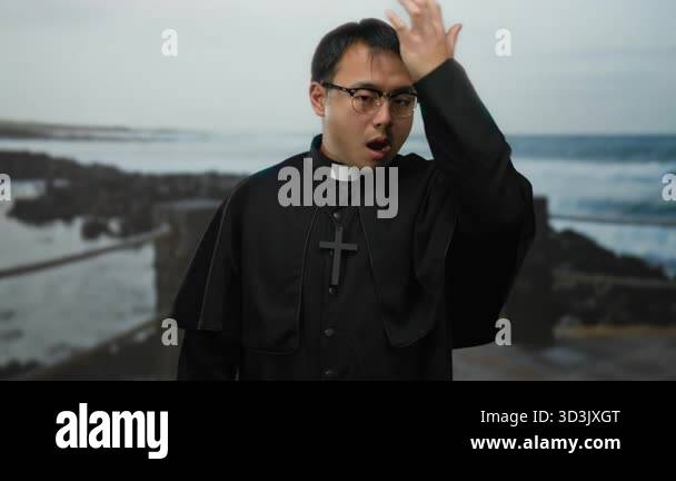 Man in priest attire stands by seaside promenade expressing emotion ...