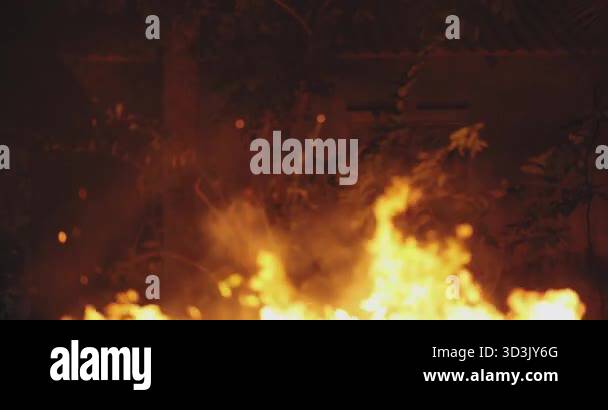 A house barely visible in the dark, illuminated by intense flames in ...