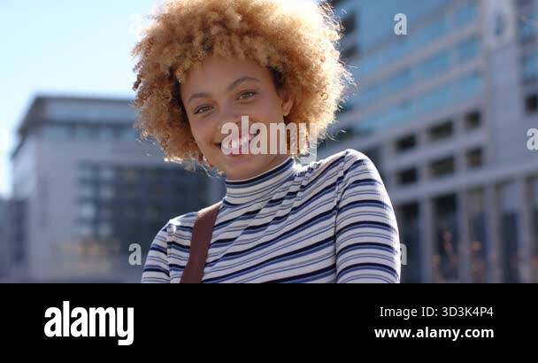 African American woman in striped sweater smiling and tilting in urban ...
