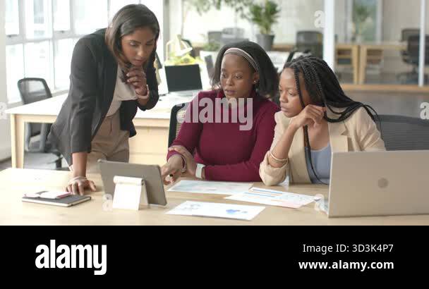 Diverse female coworkers pointing at charts, tablet, typing on laptop ...