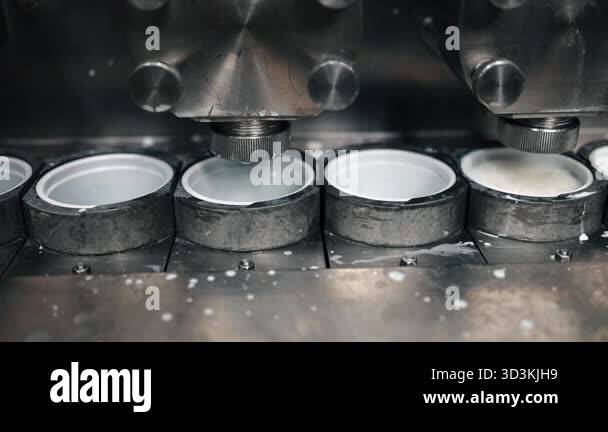 Robotic machine filling plastic cups with creamy yogurt on an ...