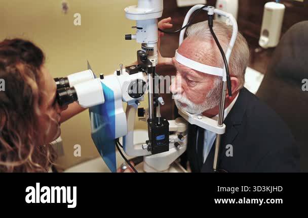 Female ophthalmologist examining a senior male patient's eyes with a ...